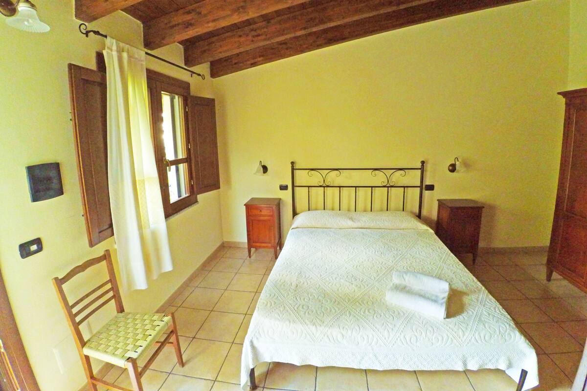 Quarto com cama, poltrona, mesa de cabeceira e teto de madeira.