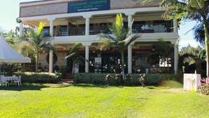 Um hotel com uma placa indicando "Gatimene Gardens Hotel" e uma área externa coberta com palmeiras e uma tenda branca.