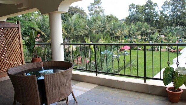 Varanda com mobiliário de vime, vista de um jardim bem cuidado e guarda-corpo branco.