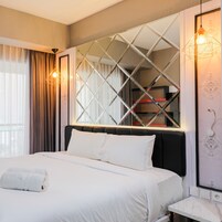 Quarto de hotel com uma cama grande, uma cabeceira moderna, um espelho decorativo e uma mesa de cabeceira com abajur.