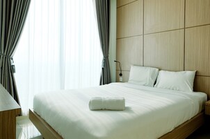 Cama bem arrumada com uma toalha enrolada, cabeceira de madeira e mesa de cabeceira com abajur.