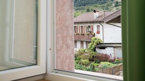 Quarto com uma grande janela com vista para uma paisagem montanhosa com casas e vegetação.