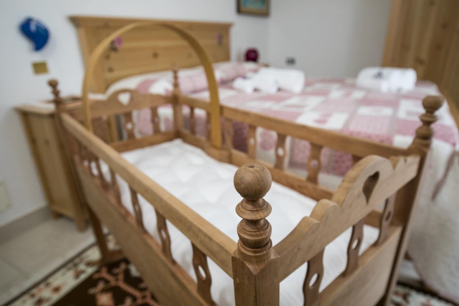 Uma cama de madeira com cabeceira e peseira, uma mesinha de cabeceira e um cobreleito estampado.