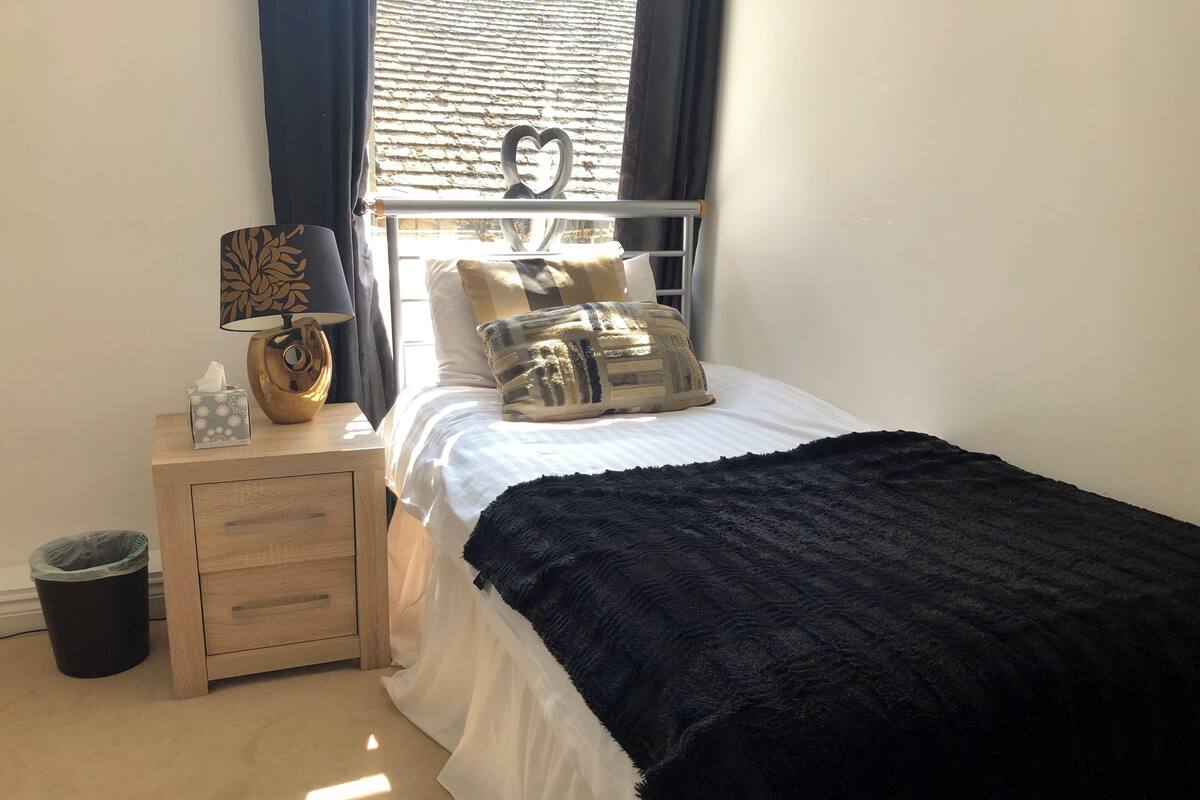 Quarto com cama, mesa de cabeceira, luminária, lixeira e janela com decoração em formato de coração.