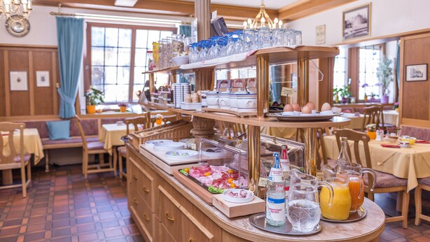 Um buffet de café da manhã com diversas opções de alimentos e bebidas, mobiliário de madeira e piso de tijolos.