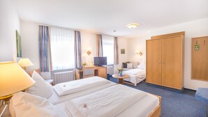 Quarto de hotel com duas camas, uma escrivaninha com computador, televisão e guarda-roupa.