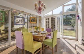 Uma sala de jantar com uma mesa de madeira, cadeiras coloridas e um candelabro.