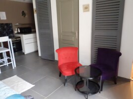 Quarto pequeno e moderno com cozinha compacta, uma cadeira vermelha, uma cadeira roxa e uma mesa de vidro.