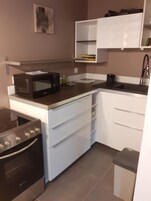 Uma cozinha compacta com micro-ondas, fogão e armários brancos.