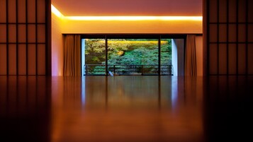 Quarto com uma grande janela, piso de madeira e vista para o verde lá fora.