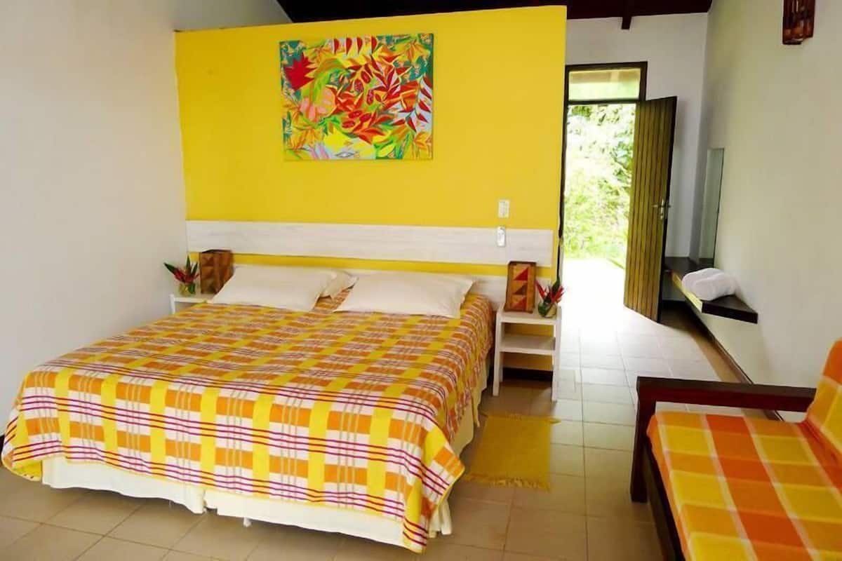 Quarto com cama, mesa de cabeceira, cadeira e um quadro na parede.