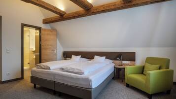 Quarto de hotel com cama grande, poltrona verde e vigas de madeira aparente no teto.