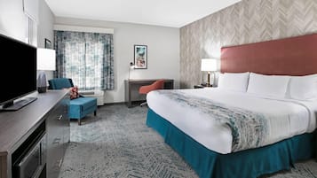Quarto de hotel com cama, escrivaninha, cadeira, televisão e janela com cortinas.