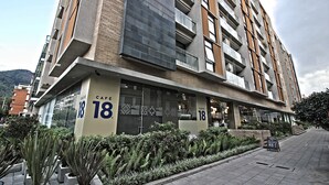 Um edifício com vários andares, com café no andar térreo, mesas ao ar livre e um jardim bem cuidado.