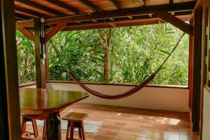 Uma rede sob uma pérgola de madeira, com vista para uma folhagem verde exuberante.