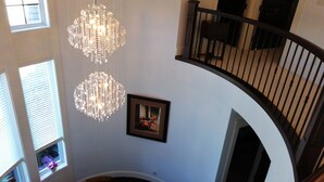 Interior com vários níveis, um lustre imponente, um quadro emoldurado e uma escadaria.