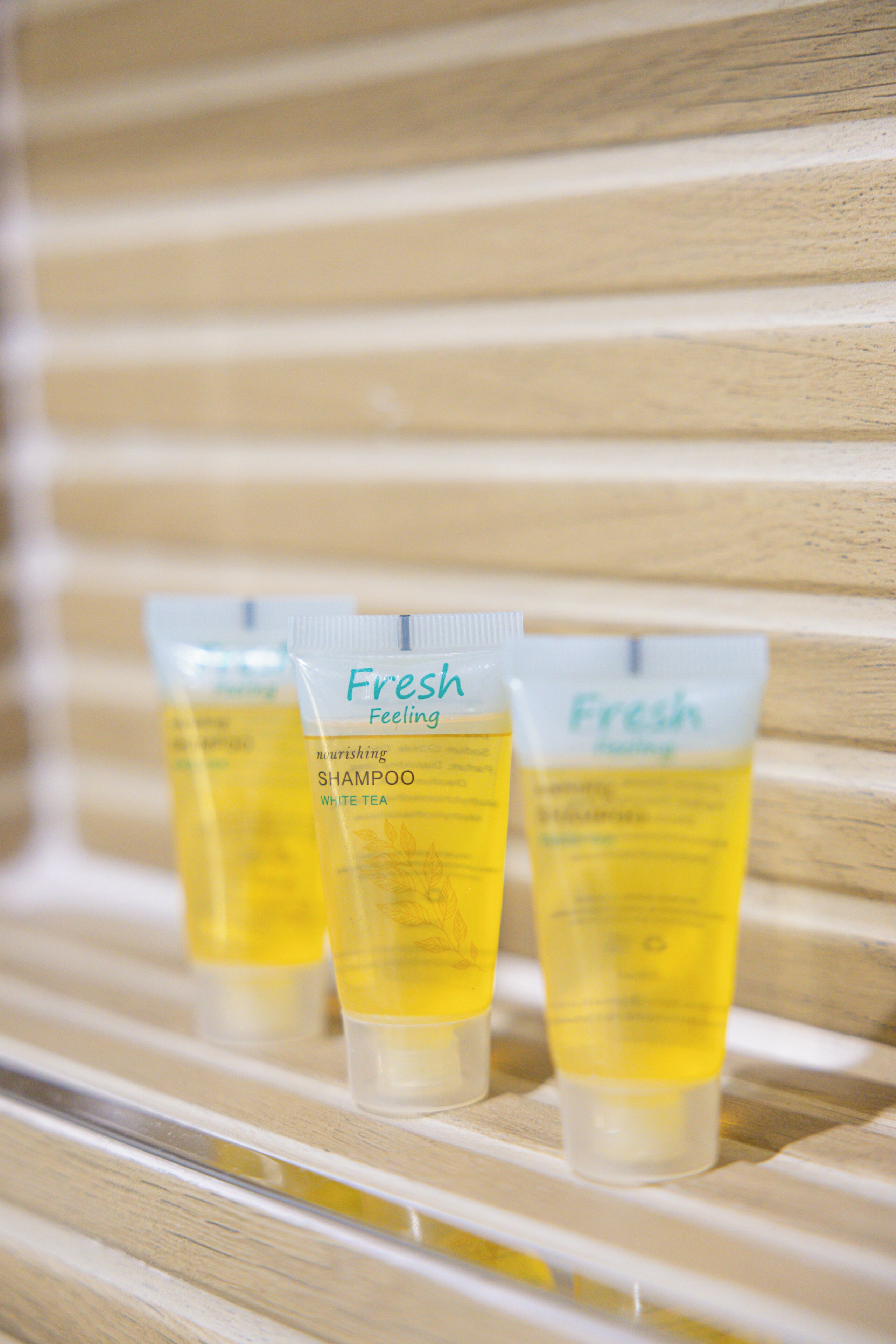 Três frascos de shampoo Fresh Feeling em uma prateleira de madeira.