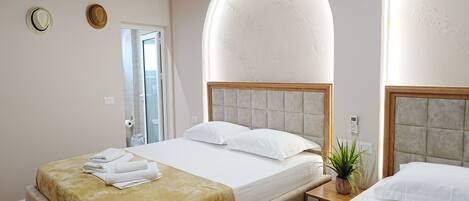 Quarto de hotel com uma cama, uma mesa de cabeceira com uma planta, um espelho e uma porta que dá para uma varanda.