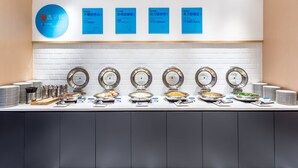 Buffet montado com várias estações de comida, cada uma com um prato de servir redondo e identificada com pratos diferentes.