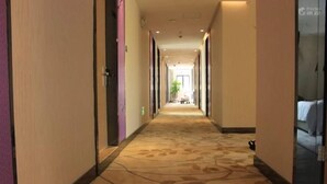 Corredor de hotel com carpete estampado, portas em ambos os lados e um banco no final.