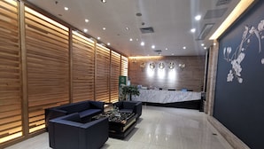Uma área de recepção moderna com balcão de mármore, painéis de madeira e um relógio fixado na parede exibindo a hora em várias cidades.