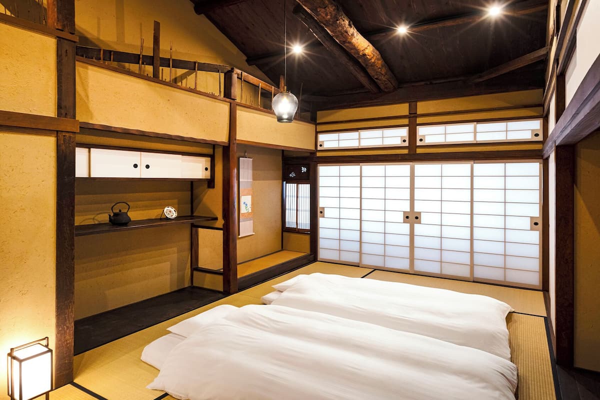 Um quarto japonês tradicional com piso de tatame, futon, divisória shoji e prateleira de madeira com um bule de chá.