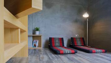Quarto moderno com piso de madeira, duas poltronas com almofadas estampadas, uma pequena estante com uma planta e um abajur.