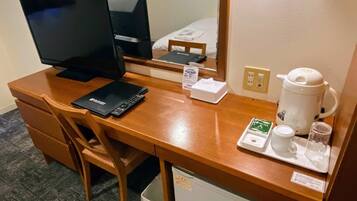 Quarto de hotel com escrivaninha de madeira, laptop, comando remoto, máquina de café e bandeja com xícara e copo.