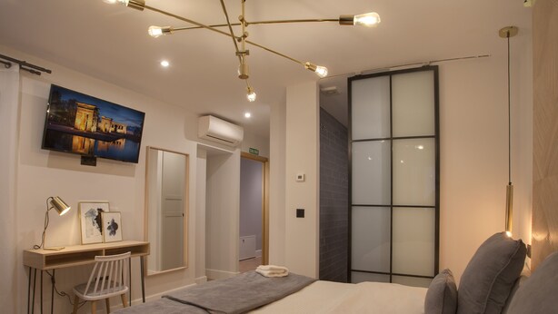 Quarto moderno com cama grande, escrivaninha, cadeira e televisão na parede.