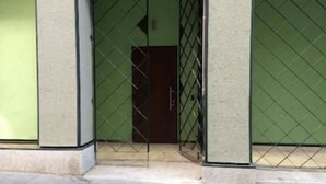 Um edifício com entrada fechada, um portão de metal e um pequeno defensivo na calçada.