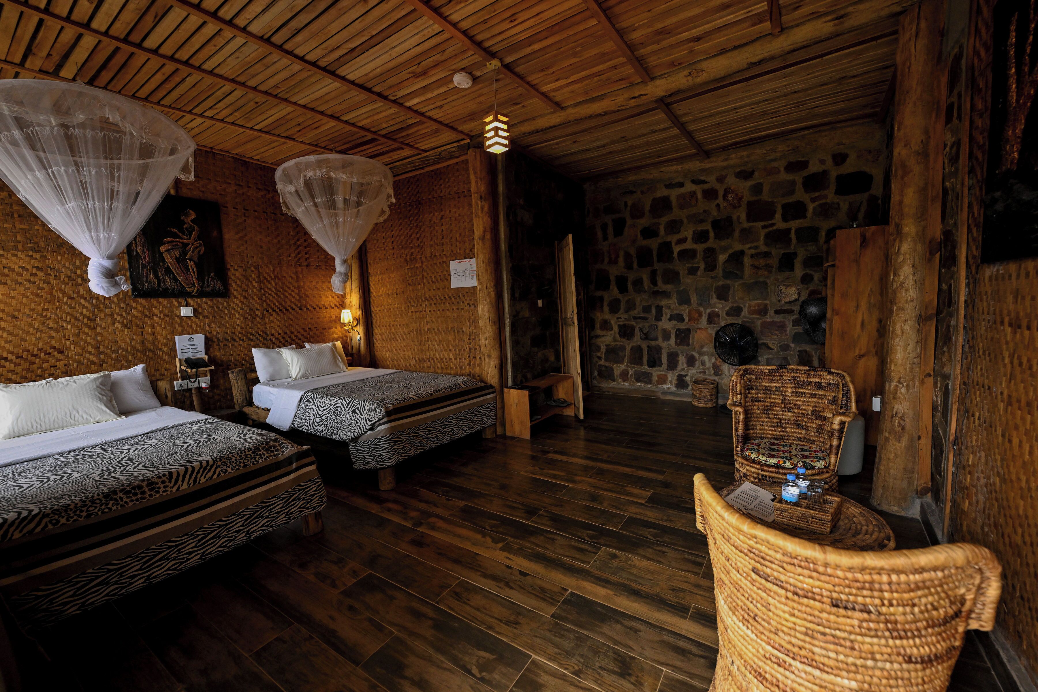 Quarto com duas camas, parede de pedra, cadeira de fibra e teto de madeira.