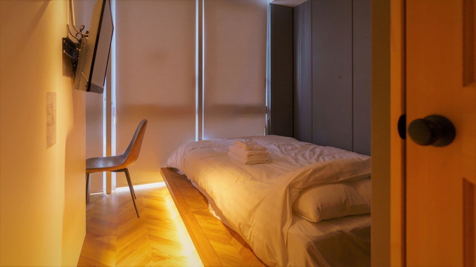 Quarto pequeno e moderno com cama, cadeira e janela.