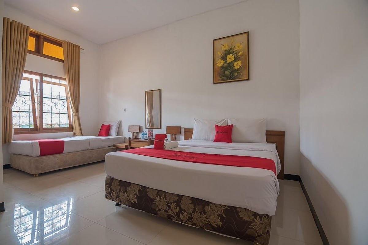 Quarto de hotel com uma cama grande, uma cama menor, uma janela com cortinas, um quadro na parede e uma mesa de cabeceira com abajur.