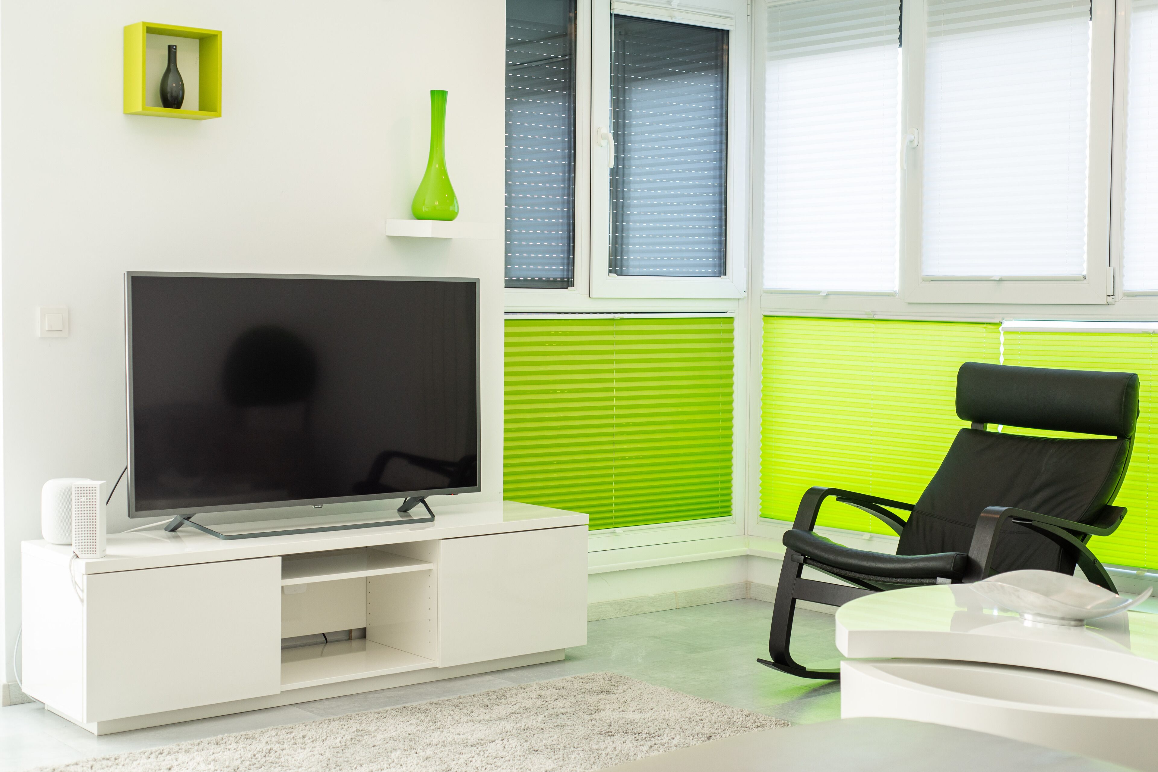 Uma sala de estar moderna com uma TV de tela plana em um móvel branco, uma cadeira de escritório preta e uma parede verde de destaque.