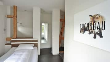 Quarto de hotel moderno com cama de madeira, parede branca com ilustração de uma raposa e vista para o exterior.