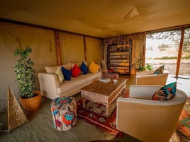 Um quarto com tenda, incluindo um sofá, poltronas, uma mesa de centro e uma estante de livros.