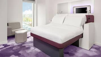 Quarto de hotel moderno com uma cama grande, área de estar e vista para a cidade.