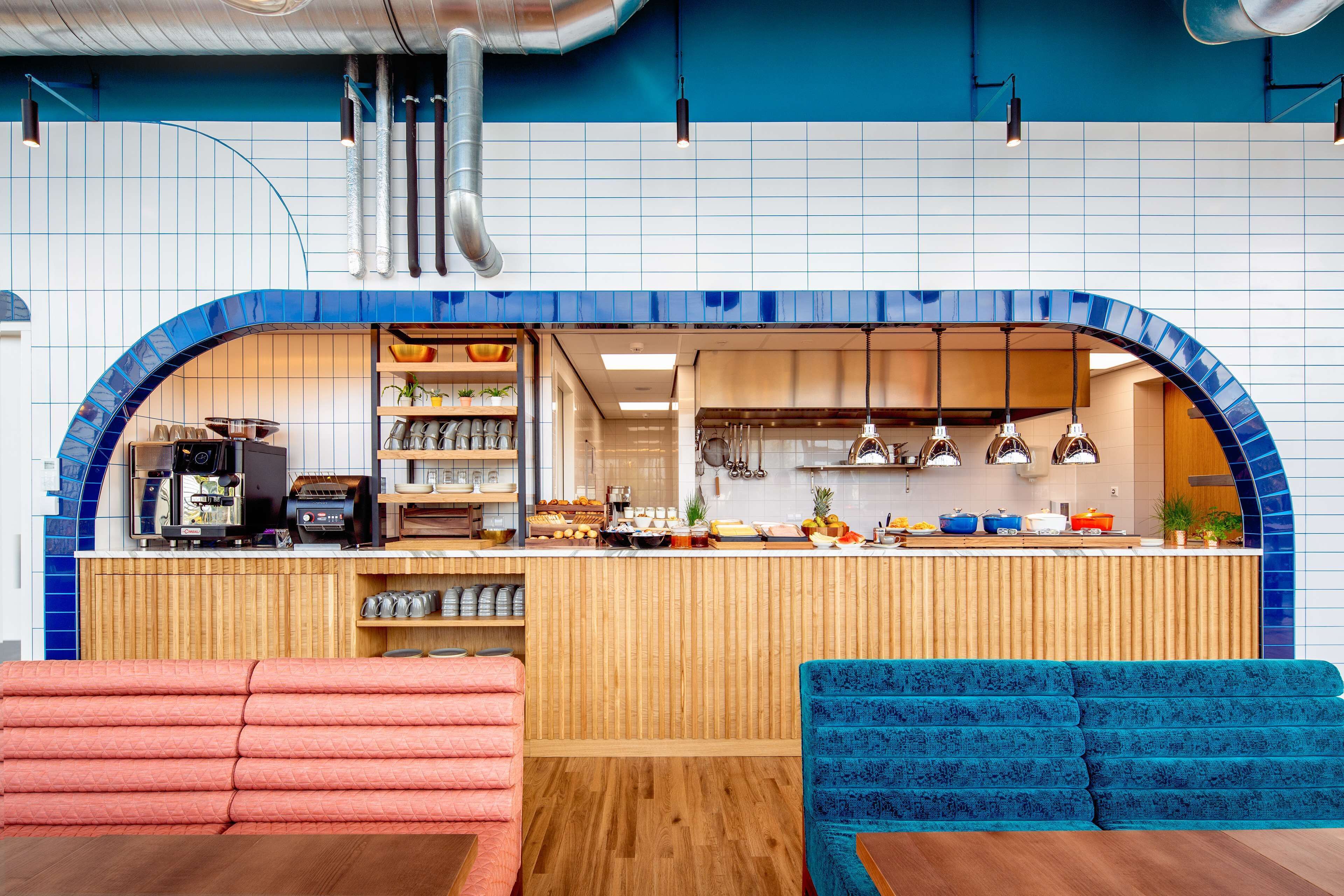 Restaurante com painel azul de azulejos, balcão de madeira e área de estar com cadeiras estofadas em rosa e azul.