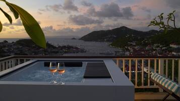 Uma varanda com dois copos de vinho, com vista para uma cidade costeira e o mar.