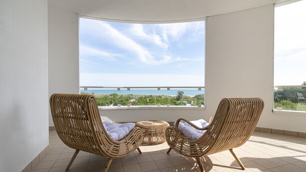 Varanda com duas cadeiras de vime e uma mesa pequena, com vista para a praia e o oceano.