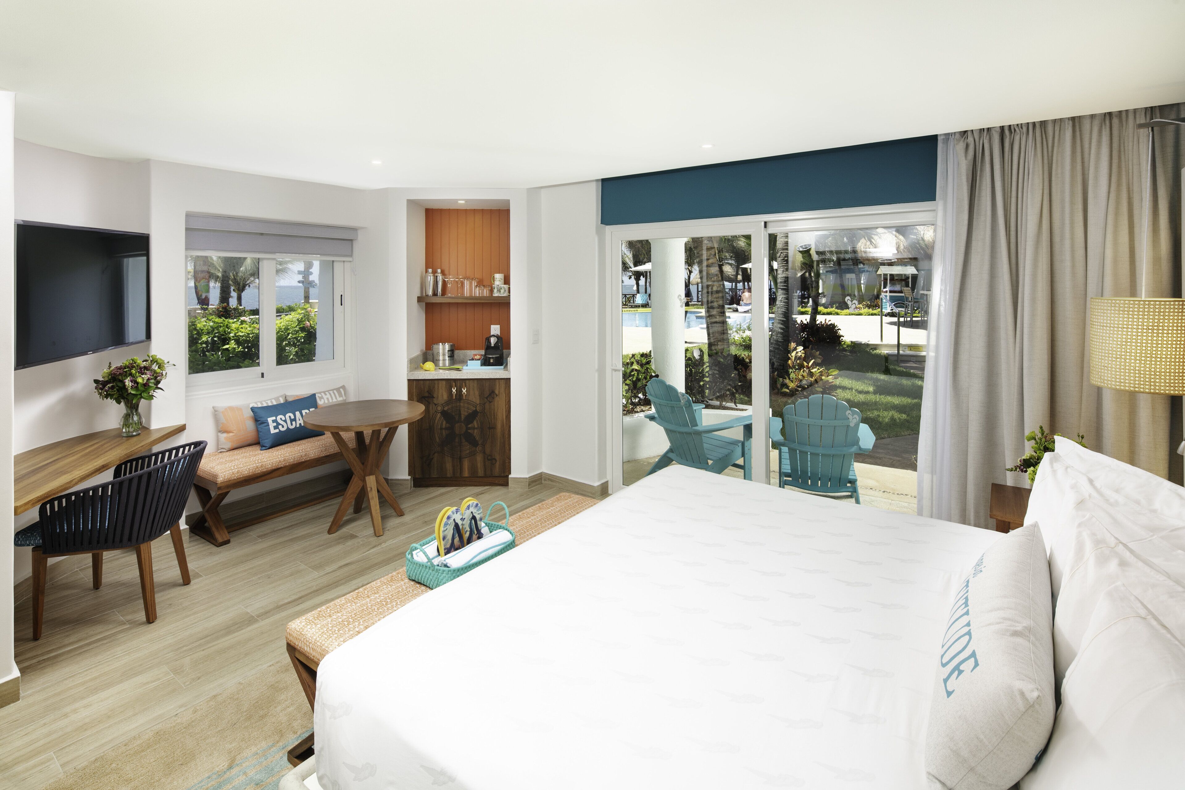 Quarto de hotel com cama, escrivaninha, cadeira, mesinha e vista para o exterior.