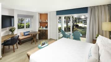 Quarto de hotel com cama, escrivaninha, cadeira, mesinha e vista para o exterior.