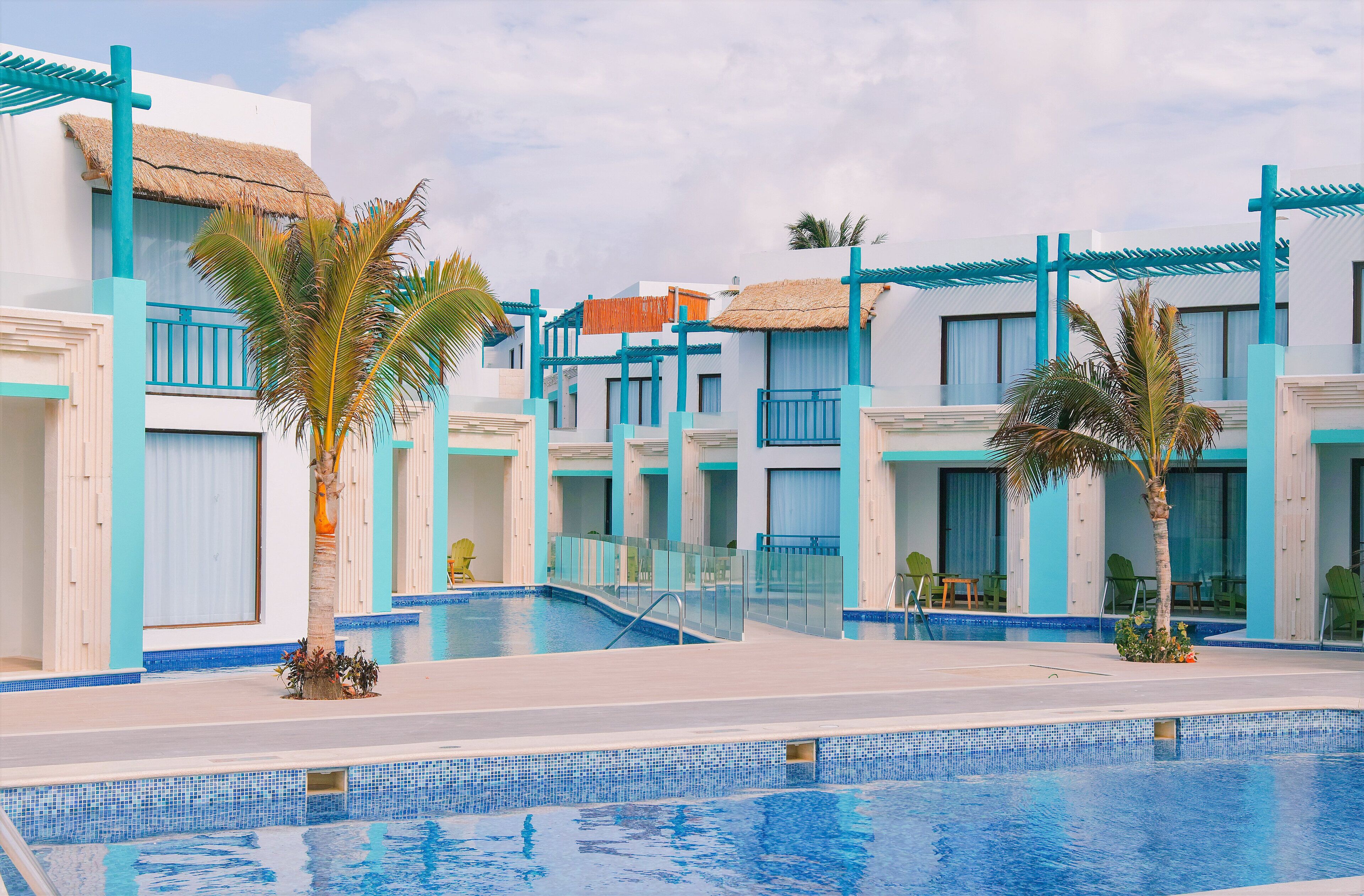 Um resort com piscina, vários quartos com varandas e palmeiras.