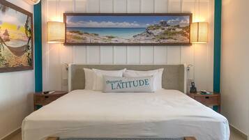 Quarto de hotel com uma cama, um quadro de uma paisagem praiana e duas luminárias fixadas na parede.