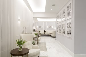 Uma sala de estar moderna com um sofá branco, uma mesa redonda com um vaso de flores e uma mesa de centro. Há quadros nas paredes e uma escada ao fundo.