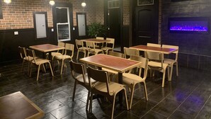 Interior de restaurante com paredes de tijolo, mesas e cadeiras de madeira, luminárias pendentes e lareira embutida.