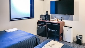 Quarto de hotel com duas camas, uma escrivaninha com computador, mini-frigorífico e televisão na parede.