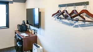 Quarto de hotel com escrivaninha, TV de tela plana, cafeteira, lixeira e cabideiro com cabides.