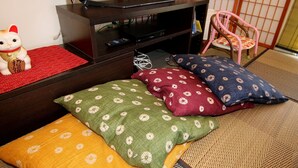 Quarto com televisão sobre suporte de madeira, uma pequena estatueta de gato e um tradicional ecrã dobrável japonês.