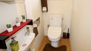 Casa de banho compacta com sanita, lavatório e uma estante com pequenas plantas em vasos.